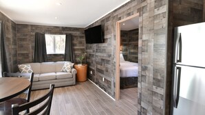 Quarto moderno com sofá, mesa de jantar, cadeiras, TV de tela plana e geladeira.