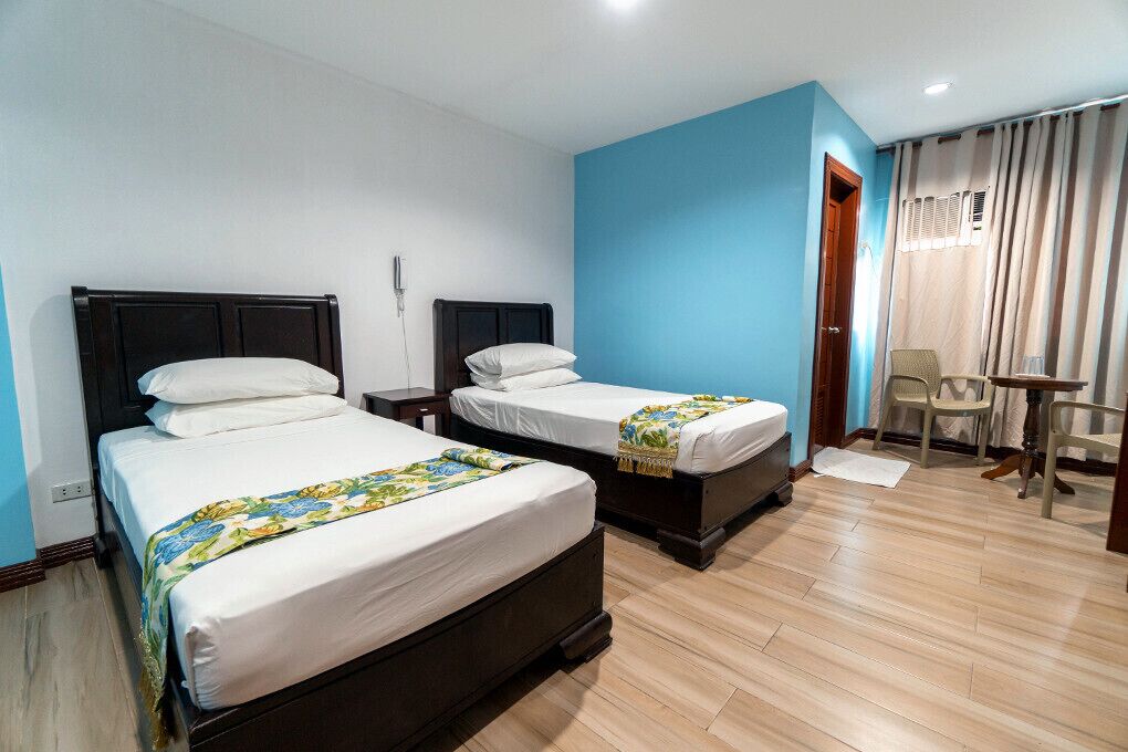 Quarto de hotel com duas camas, uma mesinha e uma cadeira.