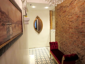 Quarto com um espelho grande, um banco vermelho, ladrilhos de chão estampados e parede de tijolos.