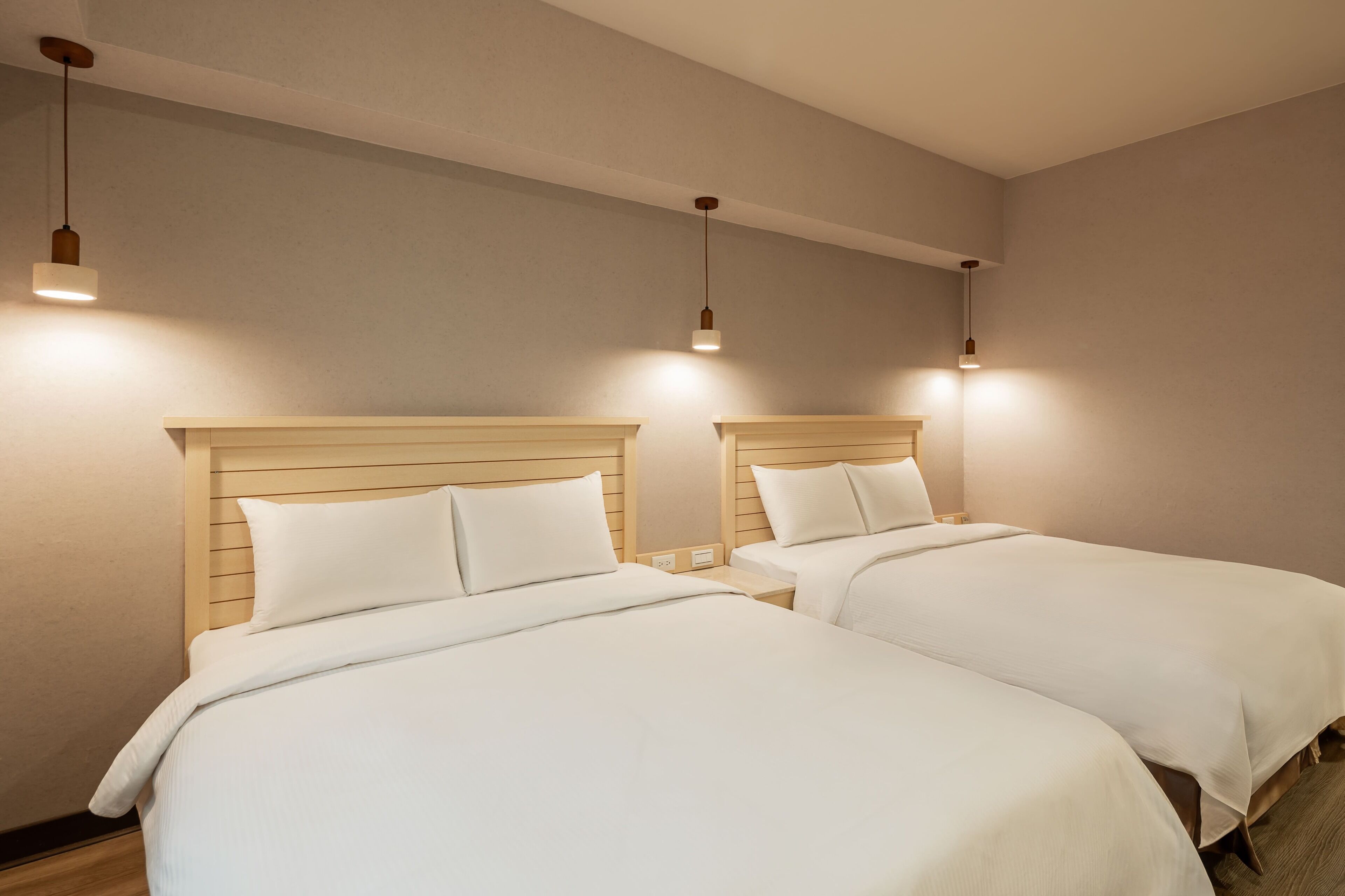 Quarto de hotel com duas camas, cabeceiras de madeira e iluminação pendente.