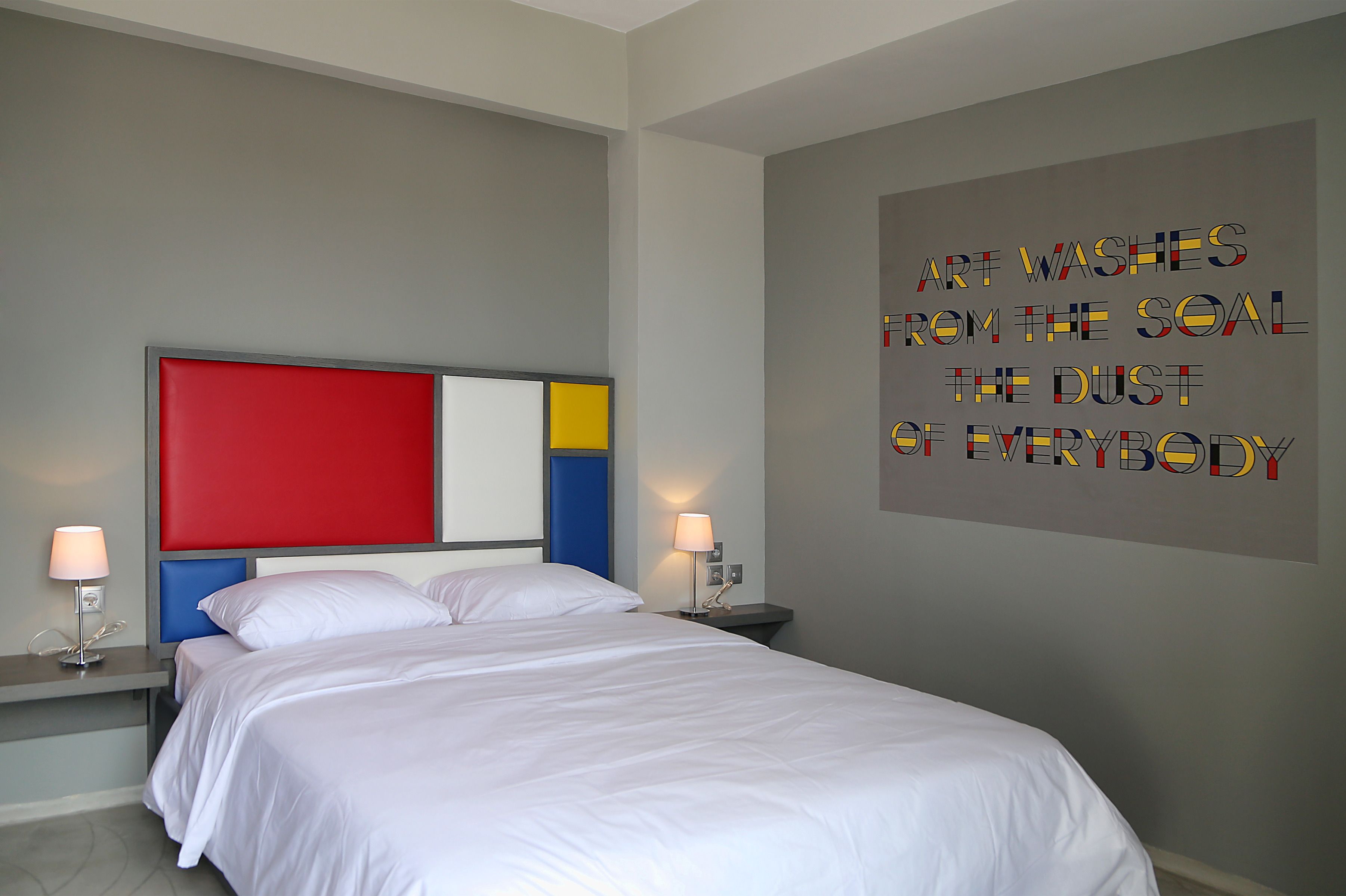 Quarto de hotel moderno com uma cama grande, duas mesas de cabeceira e uma parede com uma frase motivacional.
