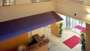Interior com vários níveis, teto de vidro, áreas de estar e plantas em vasos.