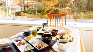 Uma refeição tradicional japonesa com diversos pratos e uma xícara de café sobre uma mesa, à beira de uma janela com vista para uma floresta.