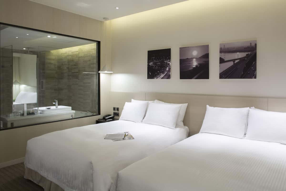 Quarto de hotel com duas camas, um espelho grande, uma mesa de cabeceira e três quadros na parede.