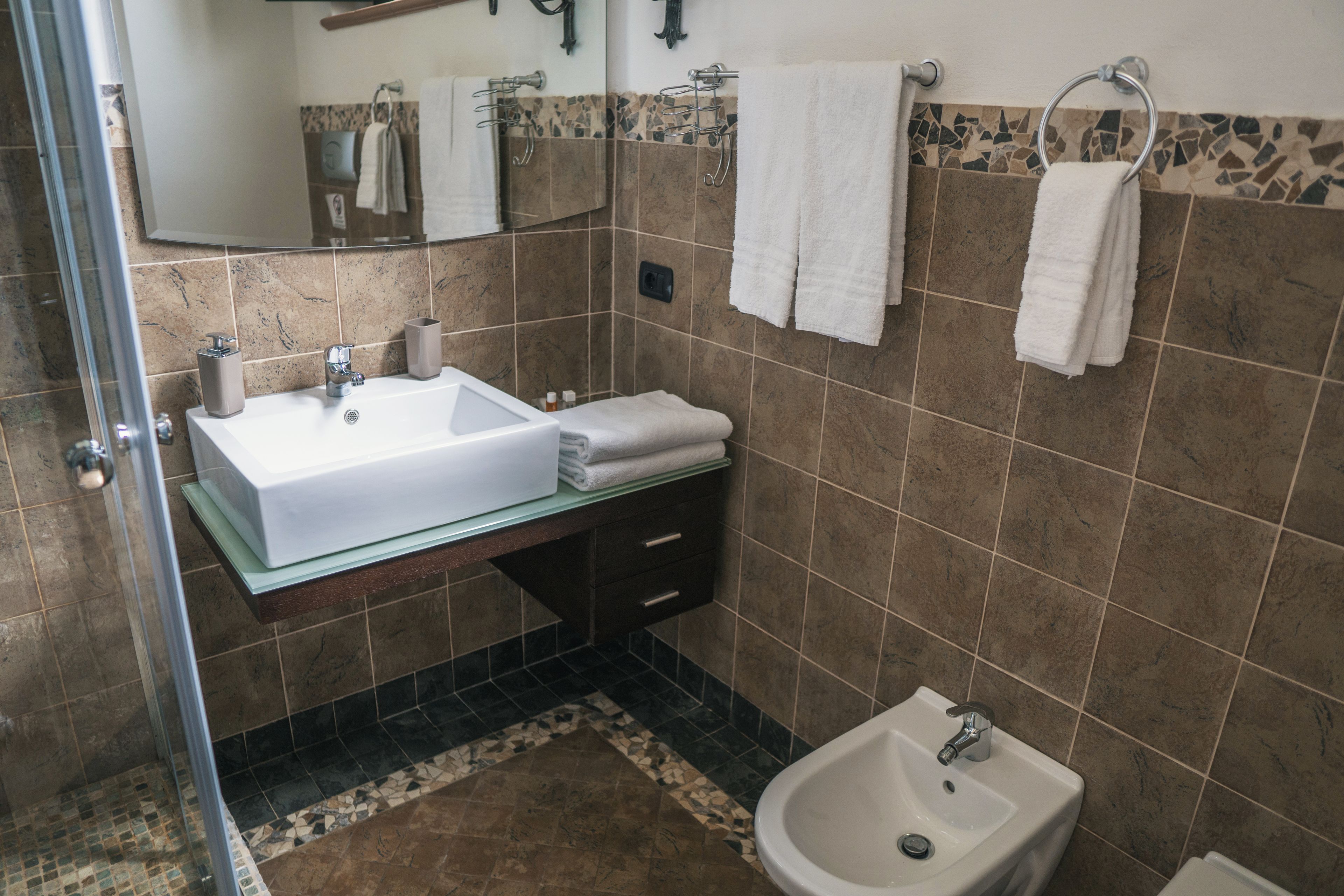 Uma casa de banho com cabine de duche em vidro, uma sanita, uma bidé e um espelho sobre a sanita.