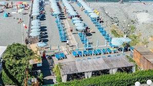 Uma praia com fileiras de guarda-sóis azuis e brancos, um bar e uma estrutura de madeira.