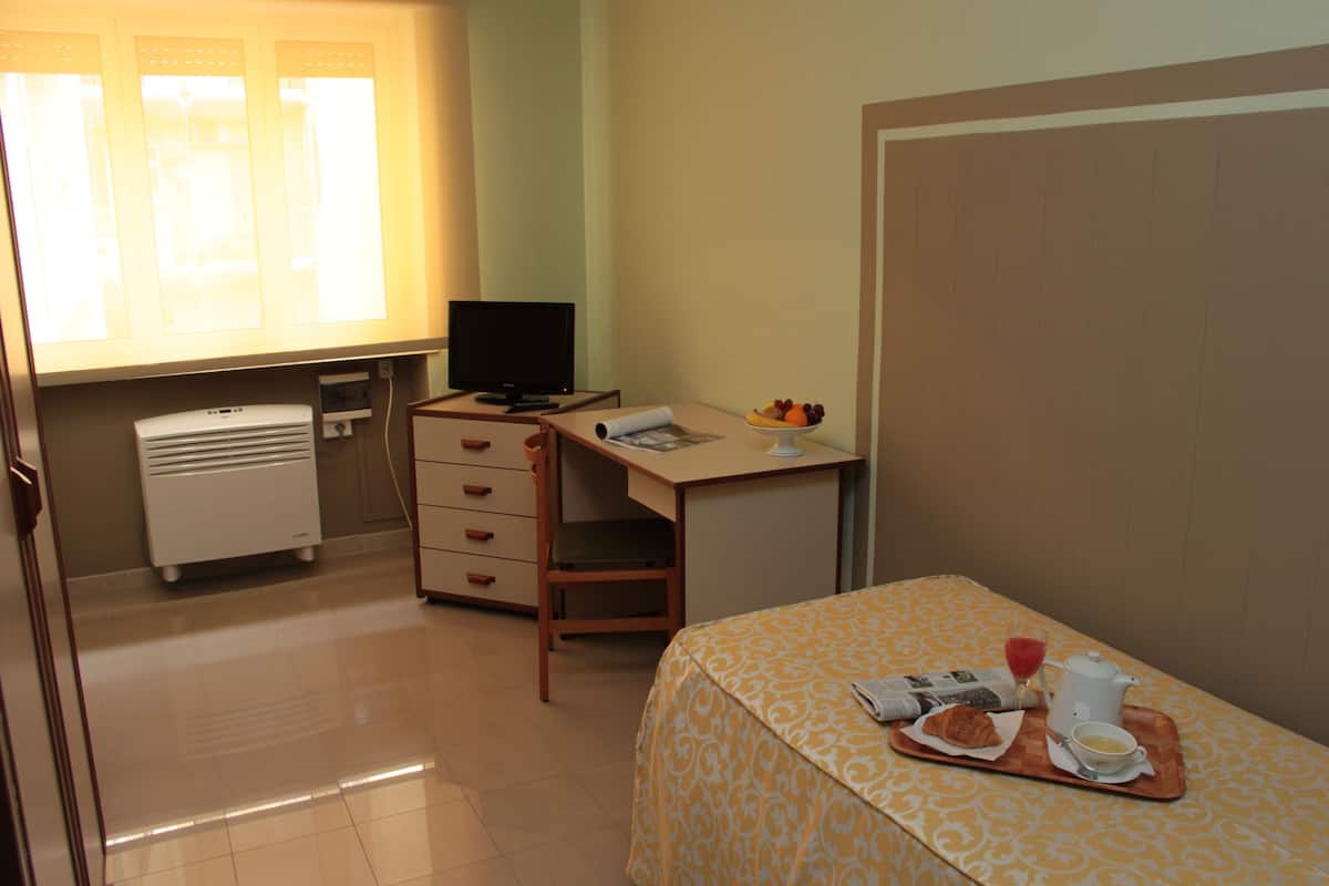 Quarto de hotel com cama, escrivaninha com computador, cadeira, radiador e bandeja com itens de café da manhã.