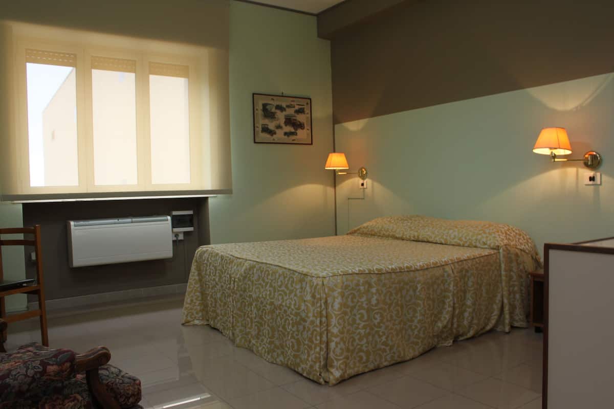 Quarto com uma cama, uma cadeira, um radiador e duas luminárias fixadas na parede.