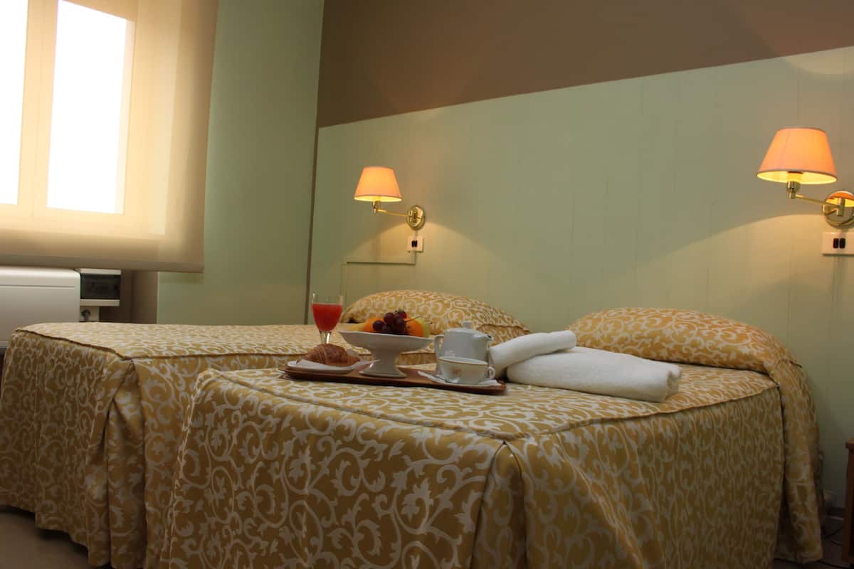 Quarto de hotel com duas camas, um suporte para o café da manhã e duas luminárias fixadas na parede.