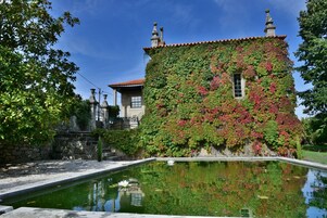 Um edifício com telhado telhado e paredes cobertas de hera, uma pequena piscina com uma flor de lótus e um céu azul límpido.