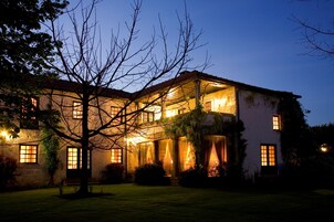 Uma casa de dois andares com varanda frontal espaçosa, várias janelas e gramado bem cuidado.