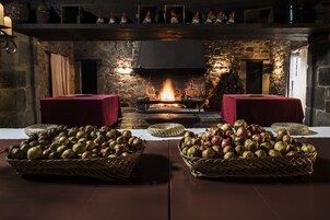 Um quarto aconchegante com lareira de pedra, duas mesas vermelhas e cestos de frutas.