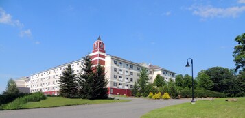 Um hotel grande, com vários andares, e uma torre vermelha e branca bem visível, cercado por vegetação e um céu claro.