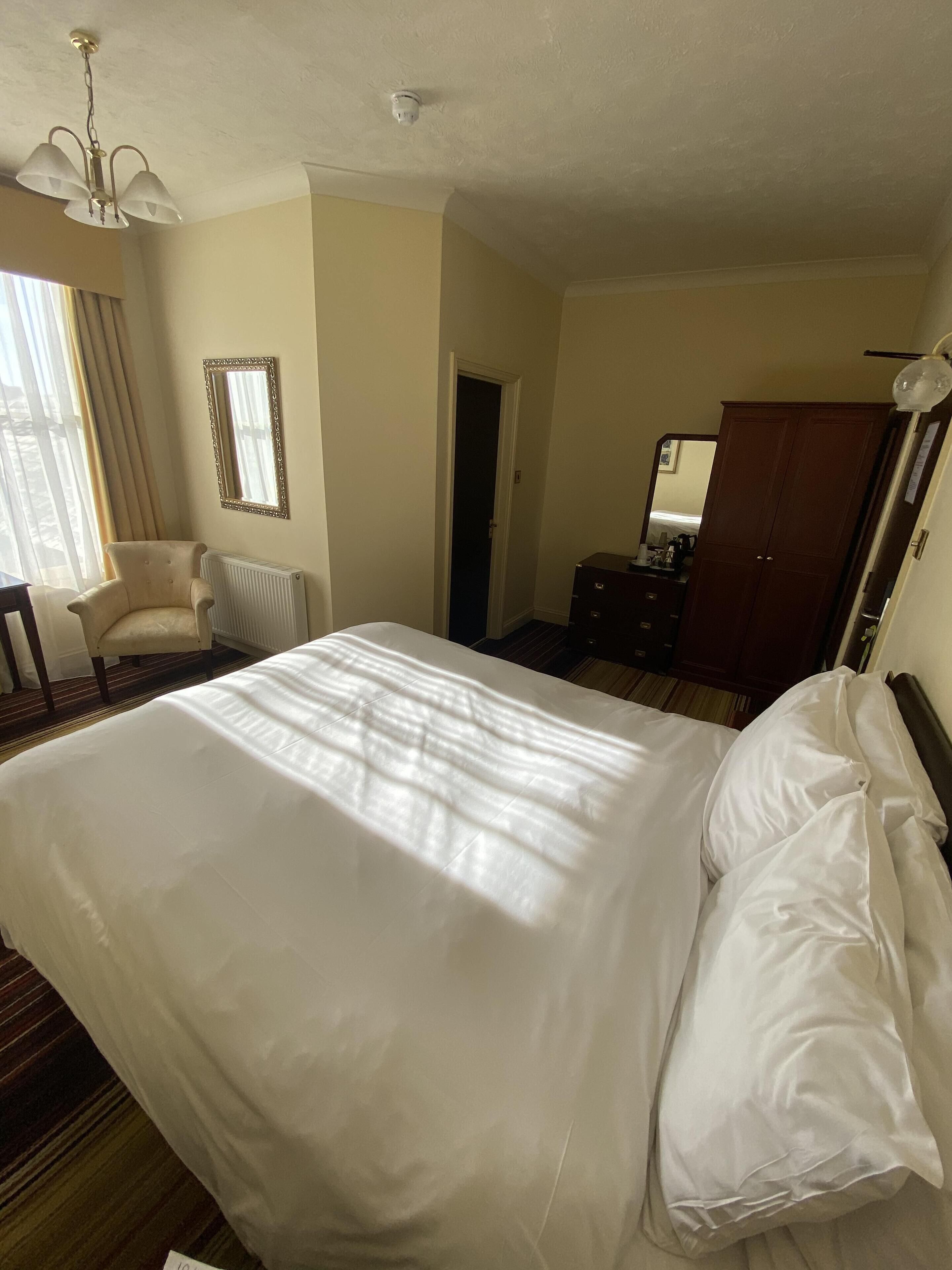 Quarto de hotel com uma cama grande, uma cadeira, uma cômoda e um espelho.