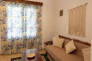 Um quarto com sofá, mesa de madeira, cortina estampada e um pendente de macramé na parede.