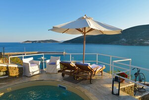Uma área na beira da piscina com espreguiçadeiras, uma mesa e um guarda-sol.