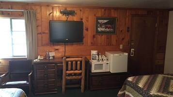 Quarto com parede revestida em madeira, televisão fixada acima de uma escrivaninha, uma cadeira, uma cama e um refrigerador.