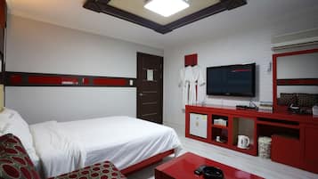 Quarto de hotel com uma cama, um aparador vermelho, uma mesa de centro vermelha e uma parede branca com uma TV de tela plana.