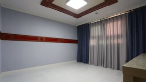 Um quarto com teto inclinado, um claraboia, uma mesa de madeira e uma janela com cortinas azuis e cinzentas.
