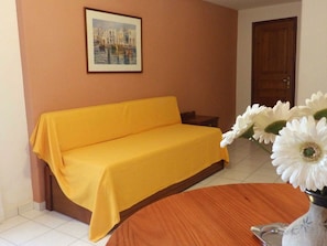 Quarto com sofá amarelo, mesa de madeira e um vaso com flores brancas.