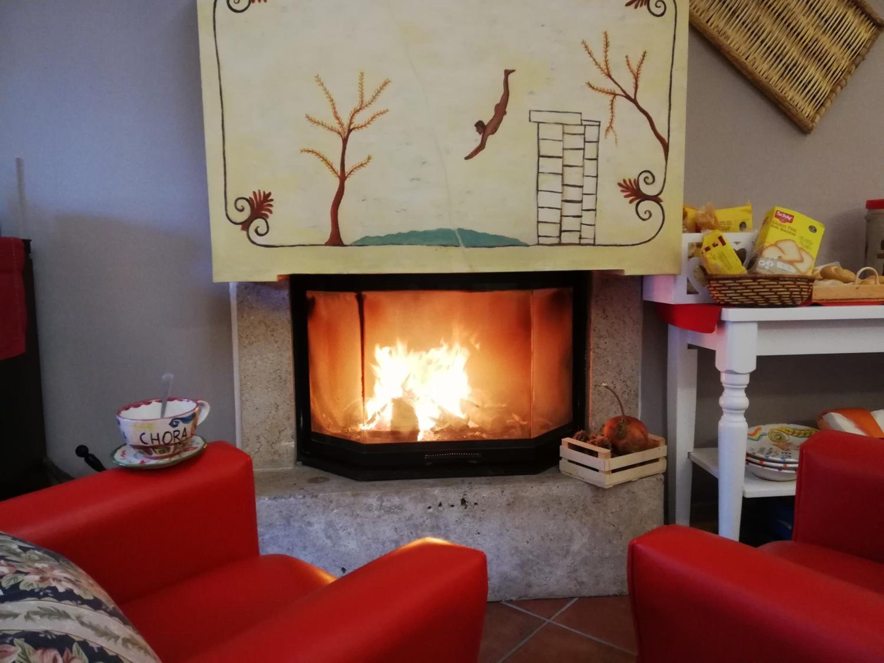 Sala de estar com lareira, cadeiras vermelhas, uma mesa com petiscos e um objeto decorativo na parede.
