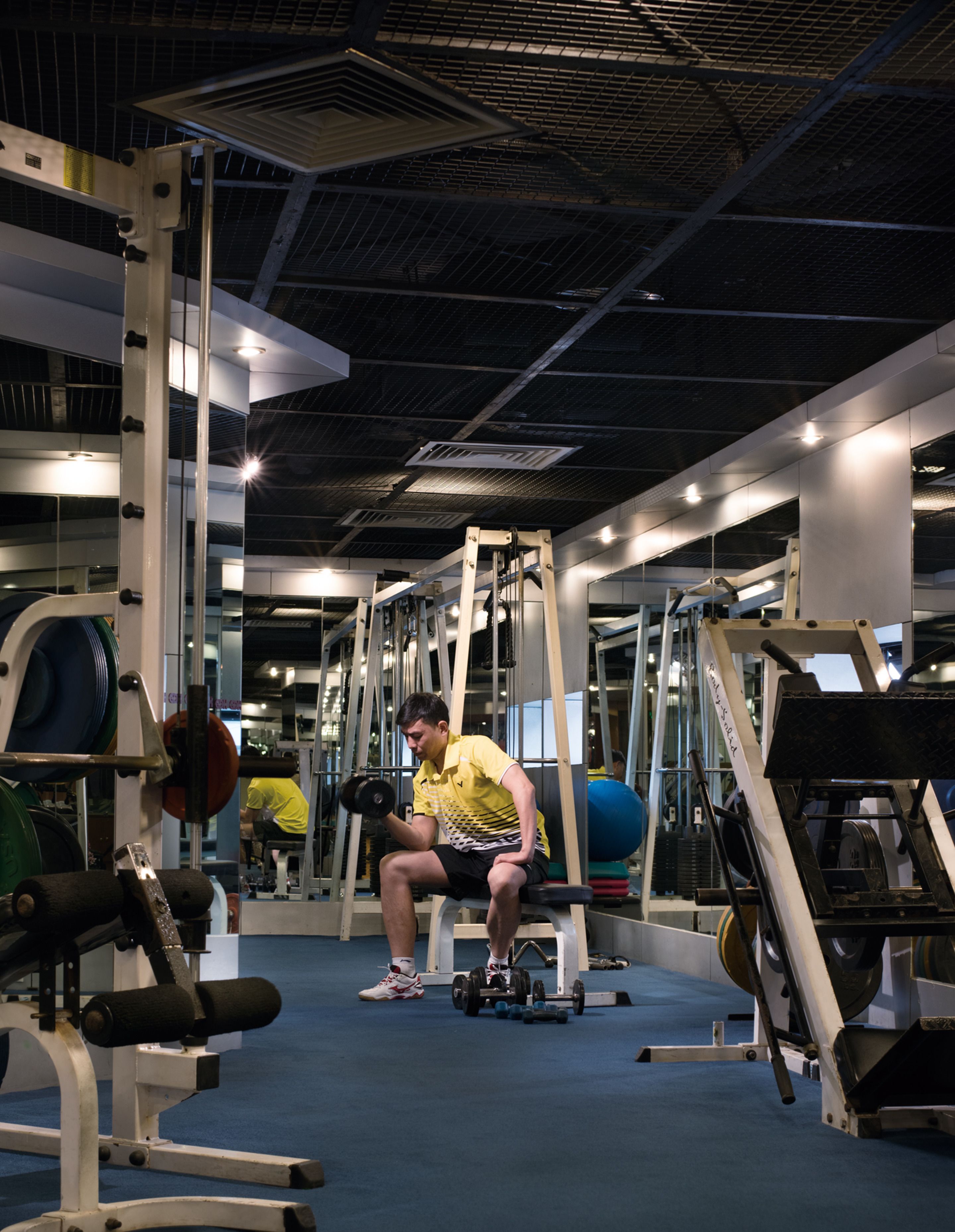Uma academia com diversos equipamentos de exercício, incluindo uma máquina de supino e suportes para pesos.