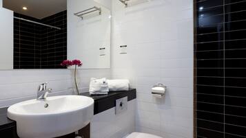 Um banheiro moderno com pia branca, bancada preta e vaso sanitário branco. Há um espelho acima da pia e um porta-toalhas na parede.