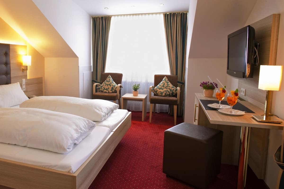 Quarto de hotel com duas camas, uma escrivaninha, uma cadeira, uma TV e uma pequena mesa com bebidas.