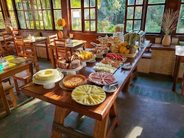 Uma mesa de buffet com diversos alimentos e vista para um jardim exuberante através de grandes janelas.