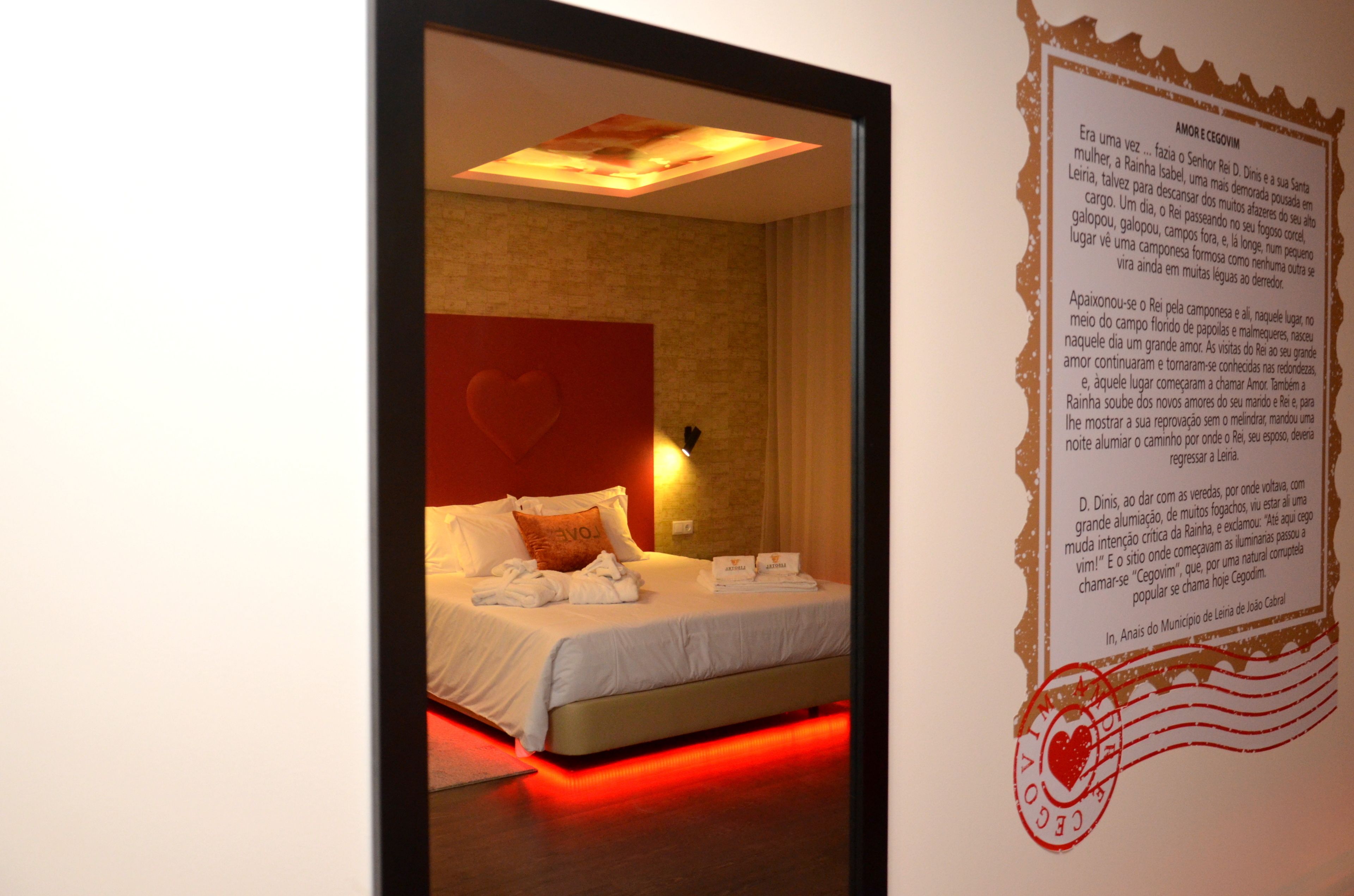 Quarto de hotel com uma cama, uma decoração em forma de coração na parede e um painel de texto na parede.