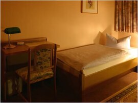Uma cama de solteiro com estrutura de madeira, uma mesa de cabeceira com abajur e uma cadeira com estampa floral.