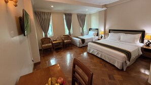 Quarto de hotel com duas camas, uma mesa de jantar com frutas e uma televisão.