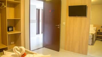Quarto de hotel com guarda-roupa de madeira, televisão fixada na parede e cama com edredom branco.