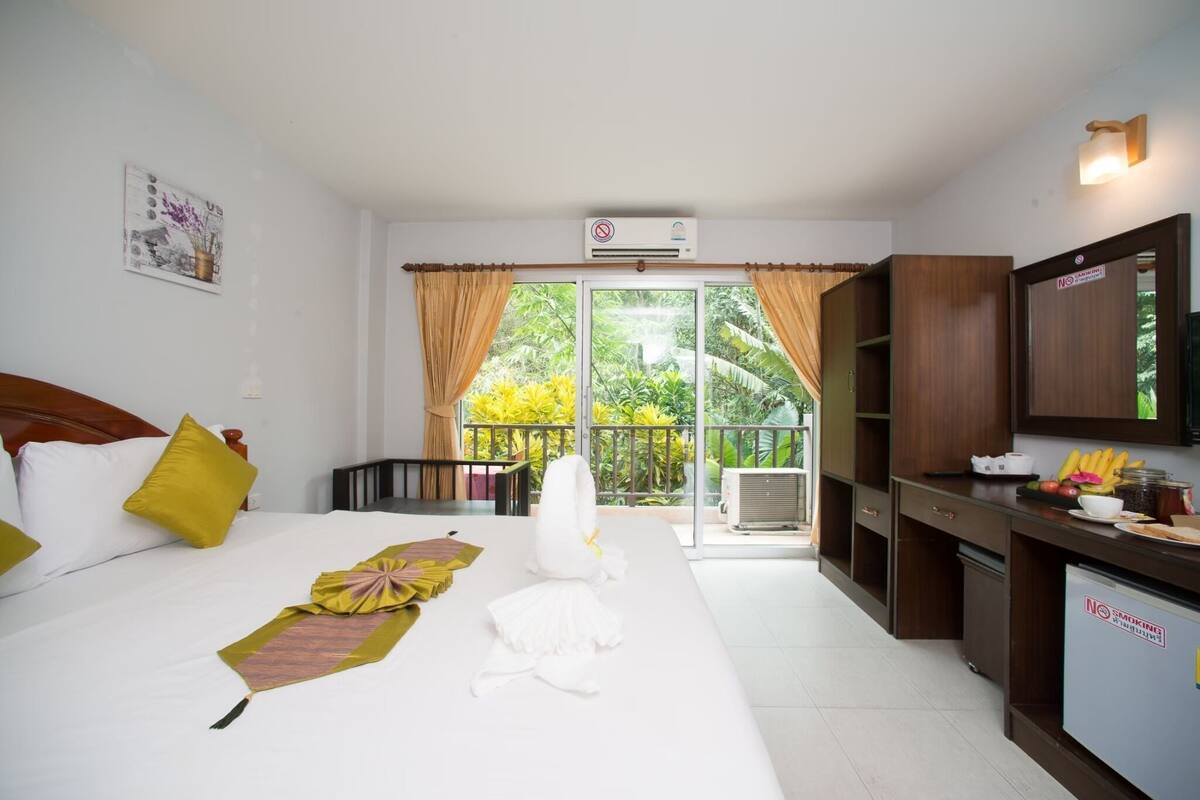 Quarto de hotel com cama, escrivaninha, cozinha compacta e varanda com vista para o verde.