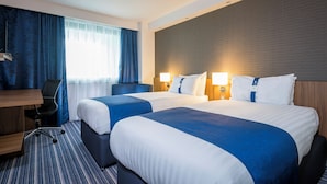 Quarto de hotel com duas camas, uma mesa e uma cadeira.
