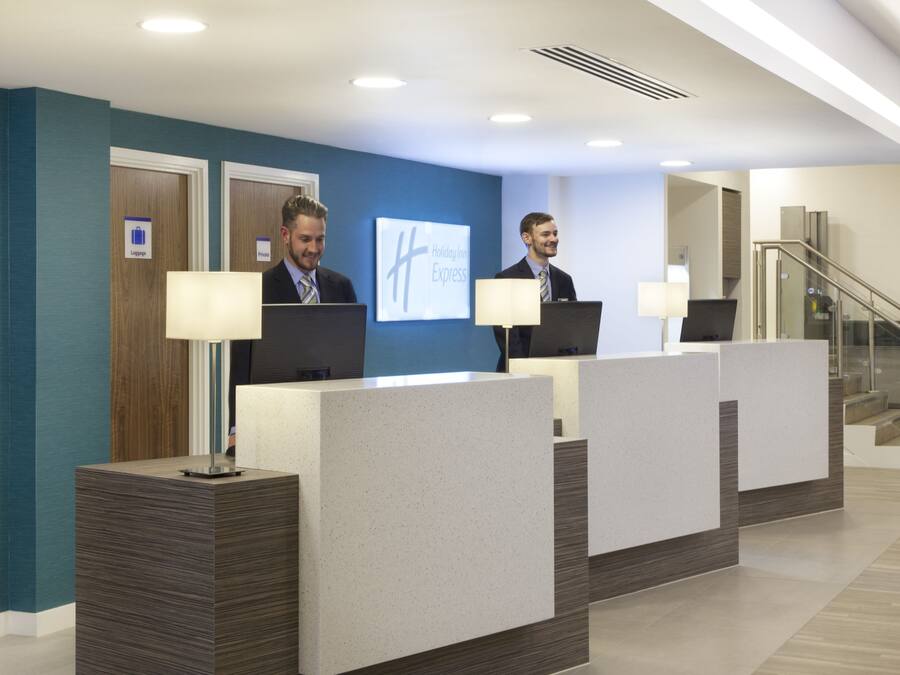 Uma área de recepção de hotel com parede azul, um letreiro Holiday Inn Express e uma escada à direita.