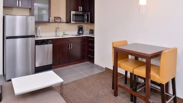 Cozinha compacta com geladeira, micro-ondas, cafeteira e uma pequena mesa de jantar para duas pessoas.