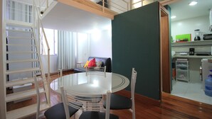 Uma sala de estar moderna com uma mesa de jantar de vidro, cadeiras brancas, um sofá e uma escada.
