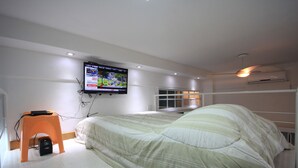 Um quarto com uma cama, uma televisão fixada na parede e um ventilador de teto.