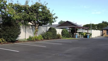 Um estacionamento com área coberta, um edifício com telhado inclinado e uma árvore.