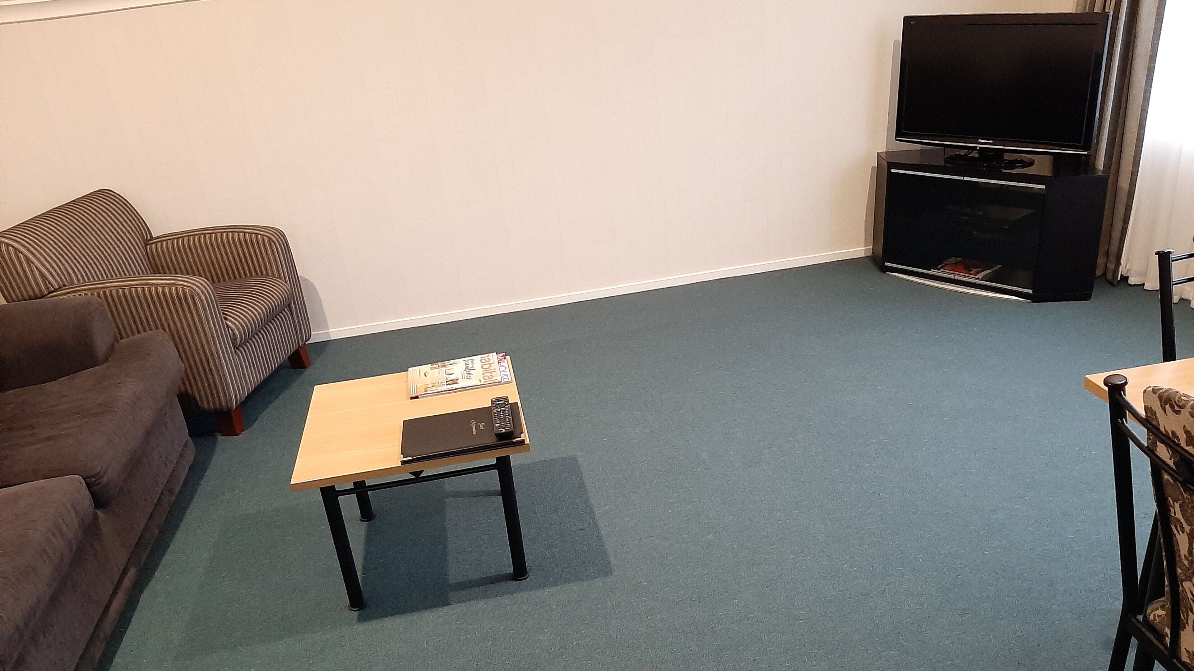 Uma sala de estar com sofá, poltrona listrada, pequena mesa de centro de madeira com revistas, televisão de tela plana em um suporte e um módulo de entretenimento preto.