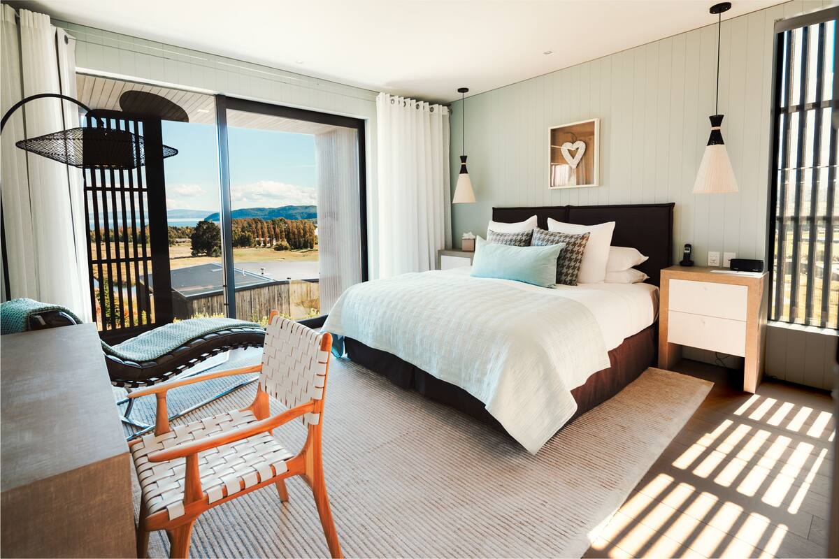 Quarto com uma cama grande, uma cadeira, uma mesa de cabeceira e vista para o exterior.