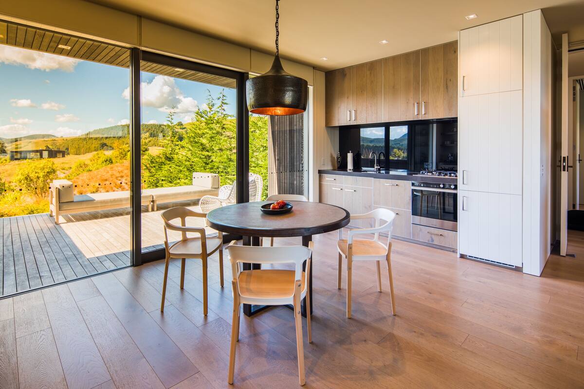 Uma cozinha moderna com armários de madeira, uma mesa de jantar redonda com cadeiras e uma janela grande com vista para uma paisagem deslumbrante.