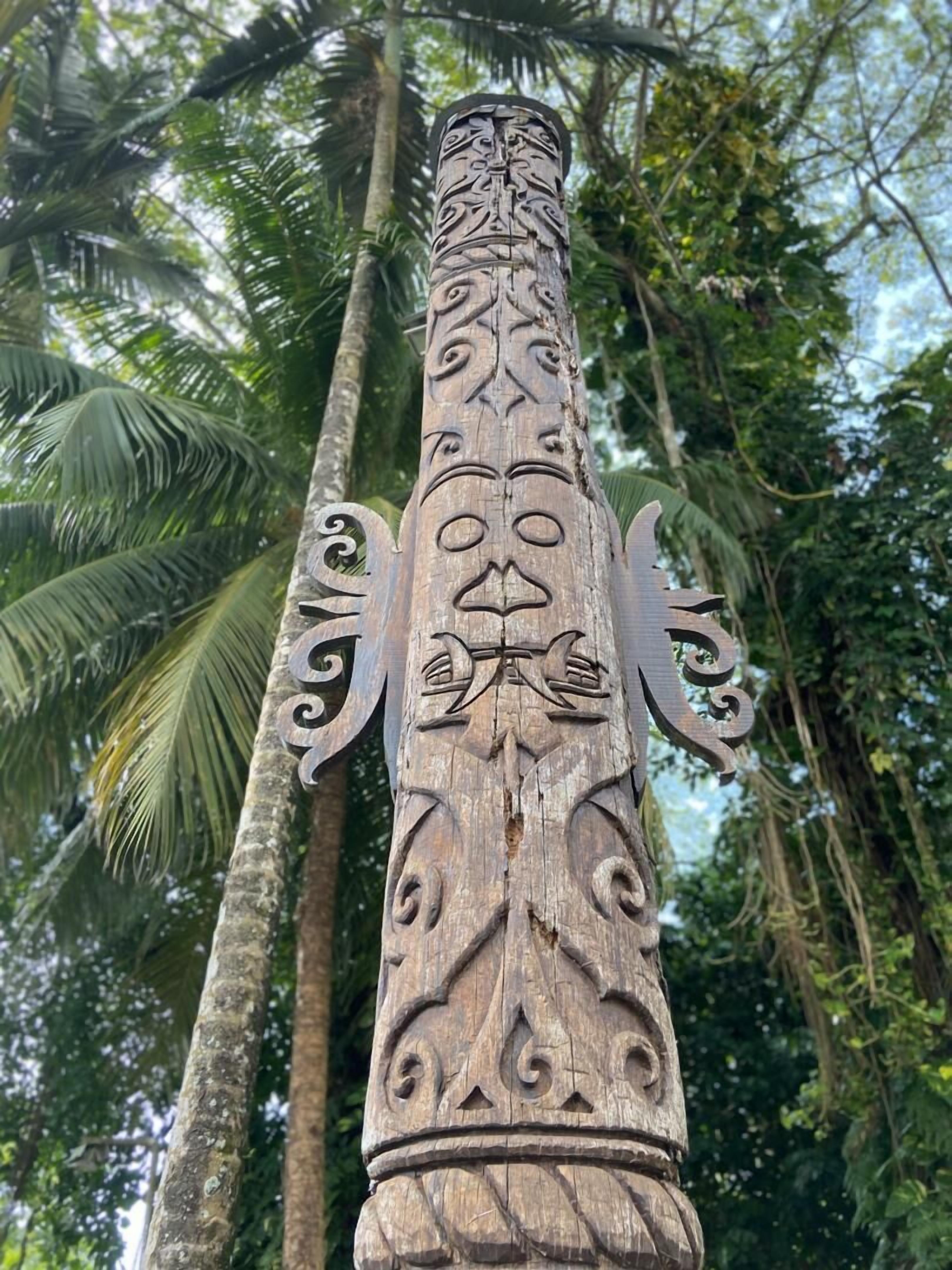Um poste de madeira entalhado com desenhos detalhados, rodeado por folhagem exuberante.