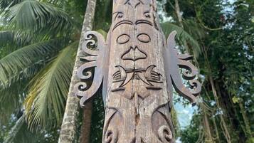 Um poste de madeira entalhado com desenhos detalhados, rodeado por folhagem exuberante.