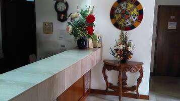 Uma área de recepção com balcão, relógio, prato decorativo na parede e uma pequena mesa com flores.