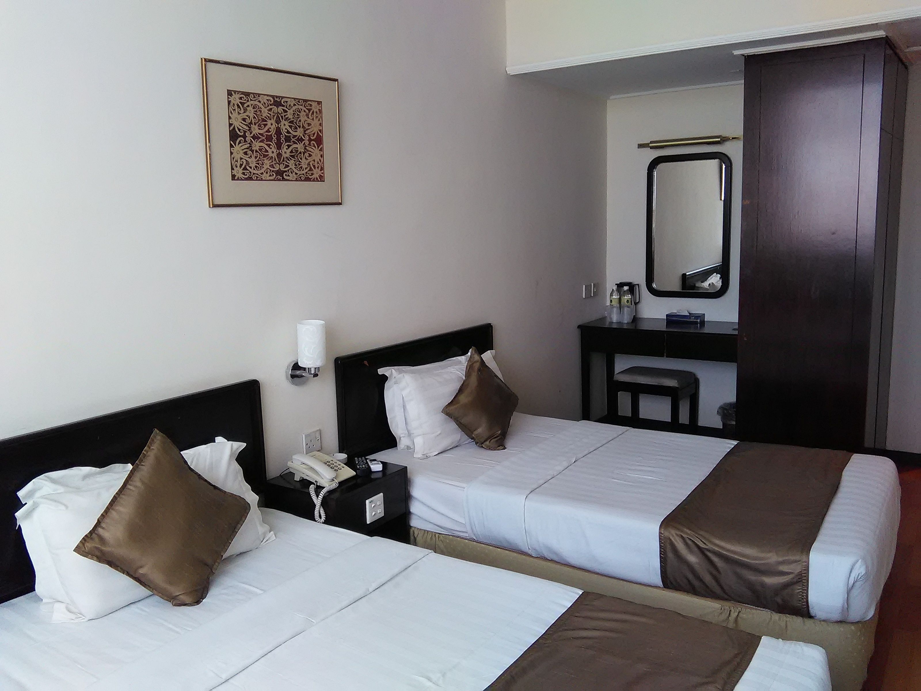 Quarto de hotel com duas camas, mesa de cabeceira com telefone, espelho e quadro pendurado na parede.