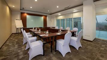 Uma sala de conferência com uma mesa grande, cadeiras brancas, um quadro branco e vista para o exterior através de grandes janelas.