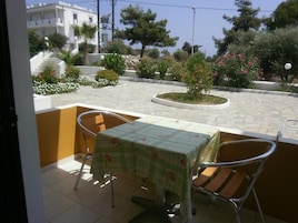Um pátio externo com mesa e cadeiras, rodeado por um jardim com diversas plantas e flores.