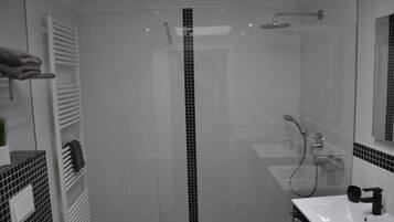 Uma casa de banho moderna com chuveiro envidraçado, lavatório branco e porta-toalhas.